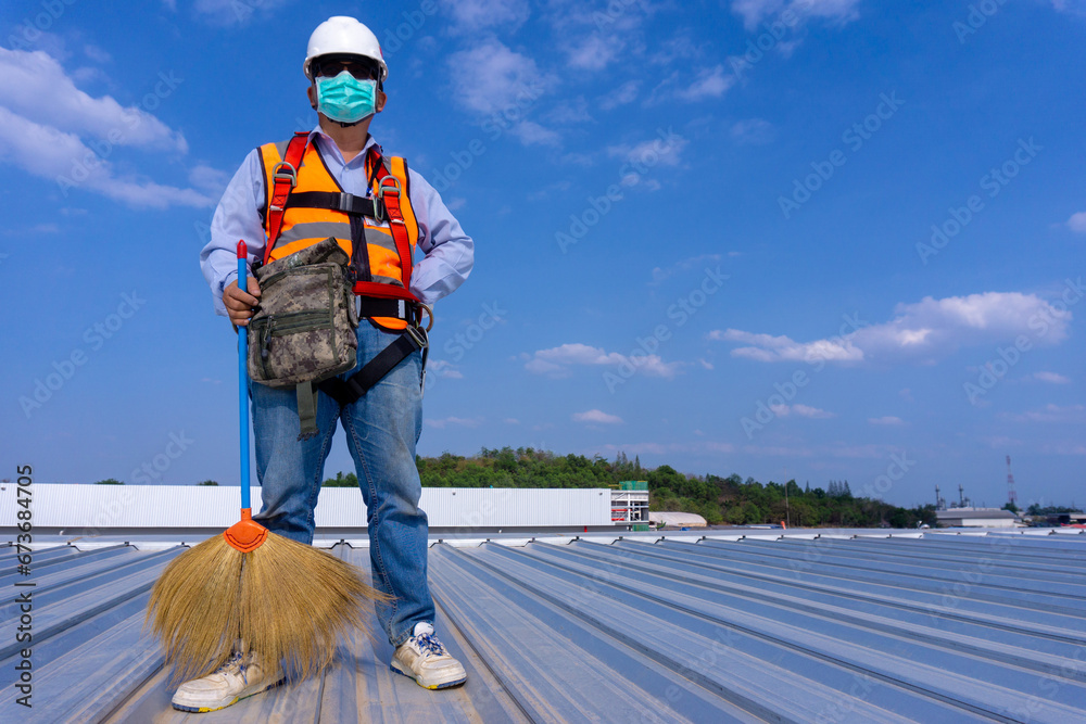 Worker wearing full safety body harness holding a broom in hand working ...