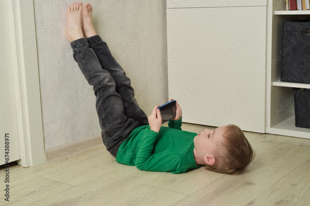 Child lies upside down on the floor and use electronics to learn, play ...