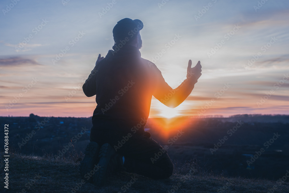 Prayer. Man on his knees praying. On the background of the sunset sky ...