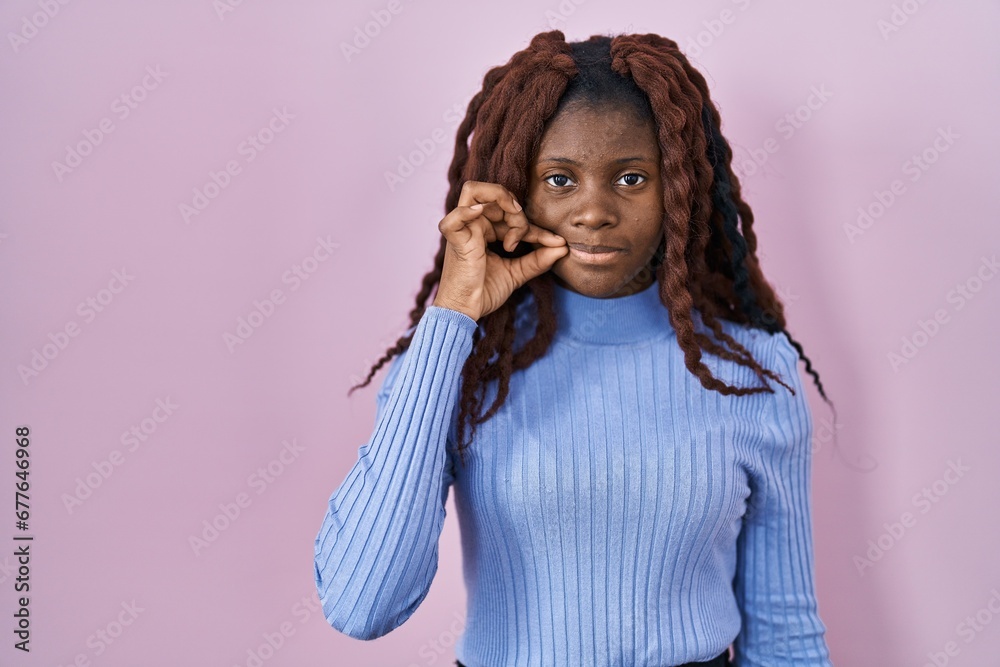 African woman standing over pink background mouth and lips shut as zip ...