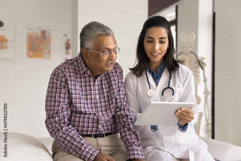 Positive young Indian doctor woman showing electronic content on tablet ...