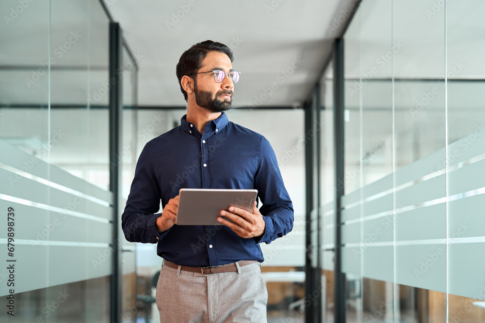 Busy Indian business man project manager looking away holding digital tablet walking in office ...