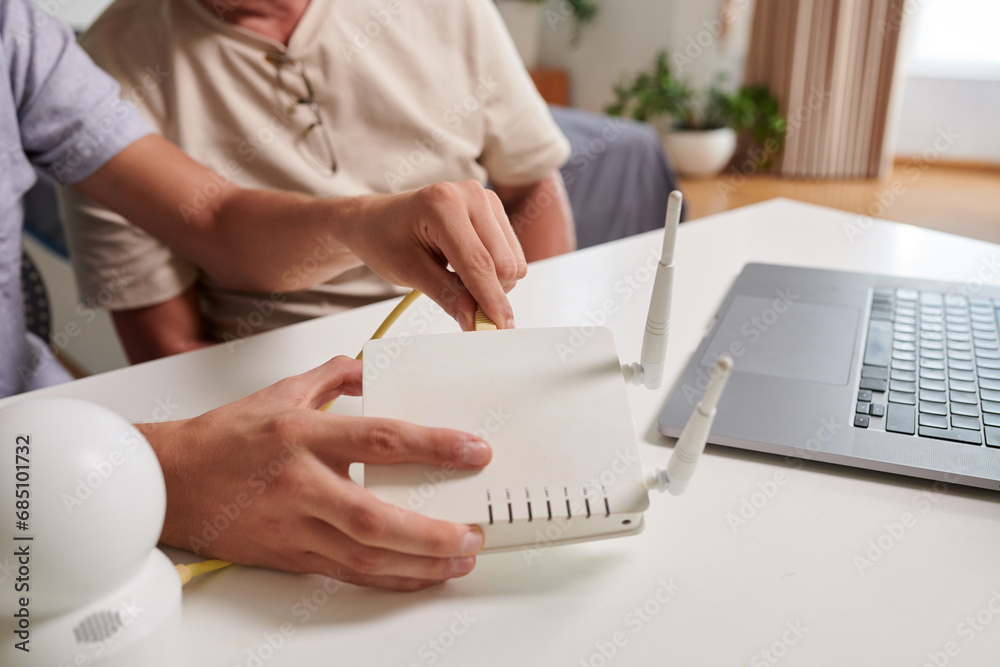 Hands of young man inserting cord in router when setting up wi-fi network in house of father ...
