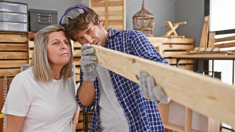 Two pro carpenters, man and woman, together looking at timber plank ...