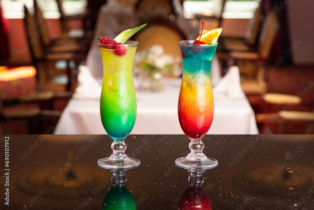 Colorful rainbow layered cocktails garnished with fruit, displayed on a ...