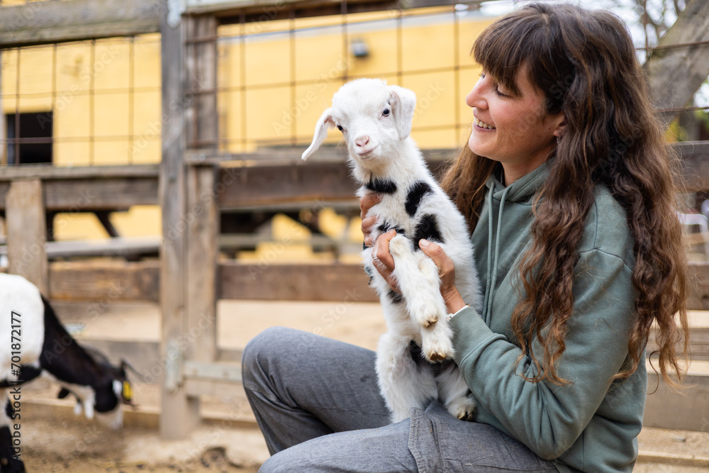 Happy young farmer woman hugging a baby goat on a rural organic farm ...