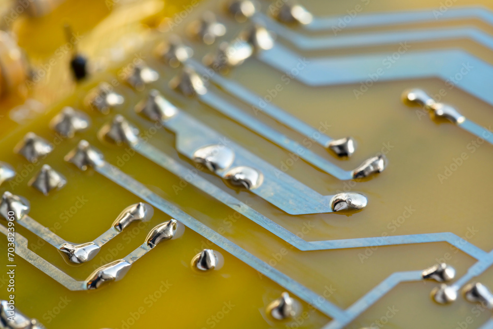 Conductor traces with silver drops of solder on a yellow electronic ...