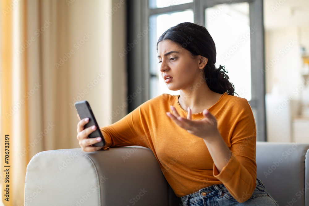 Frustrated young indian woman looking at her smartphone with gesture of ...