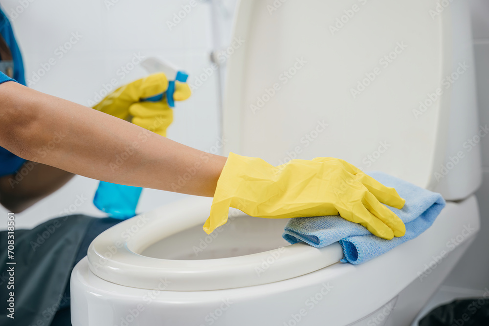 A maid in yellow rubber gloves scrubs toilet seat with cloth ensuring ...
