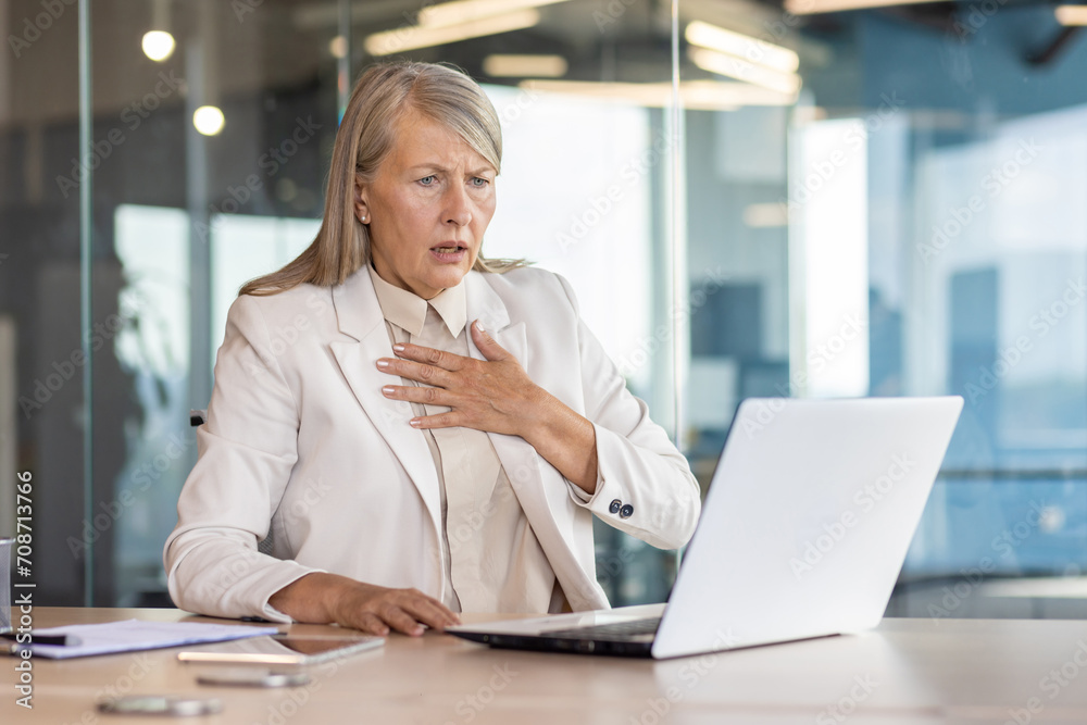 Senior woman in business suit sitting at desk in office in front of ...