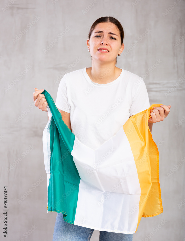 Sad young woman with Ireland flag in hands posing sorrowfully against ...