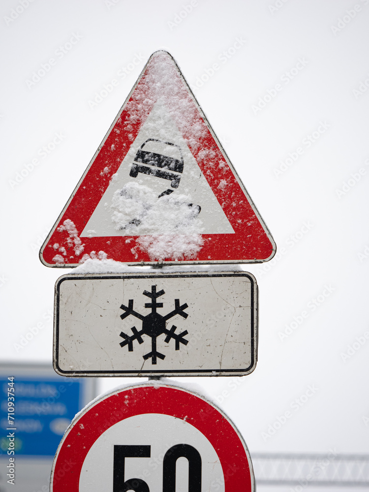 Slippery, frost warning road signs covered with snow in section with ...