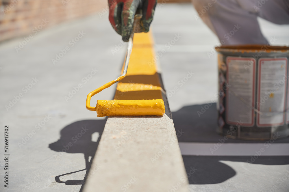 Paint roller being used to apply yellow paint on a kerbstone for road ...