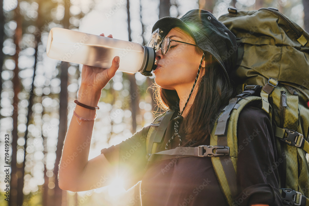 Profile photo of young woman drinking water in forest, sun flare ...