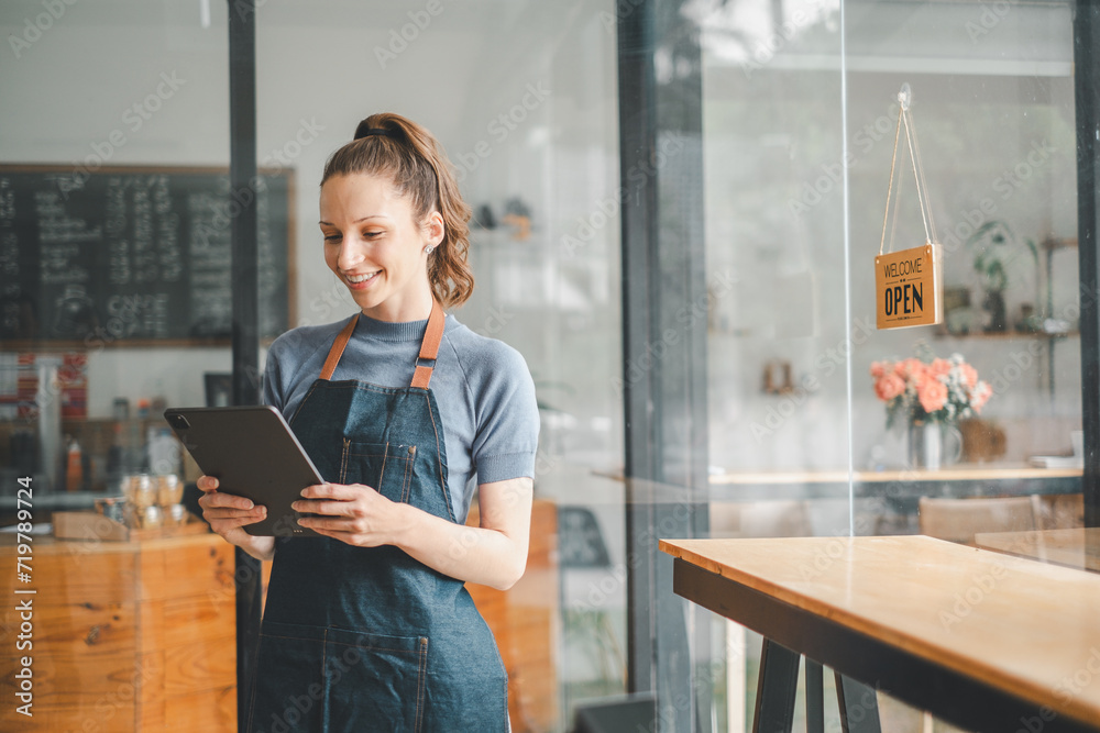 Beautiful young barista woman in apron holding tabltet and standing in ...