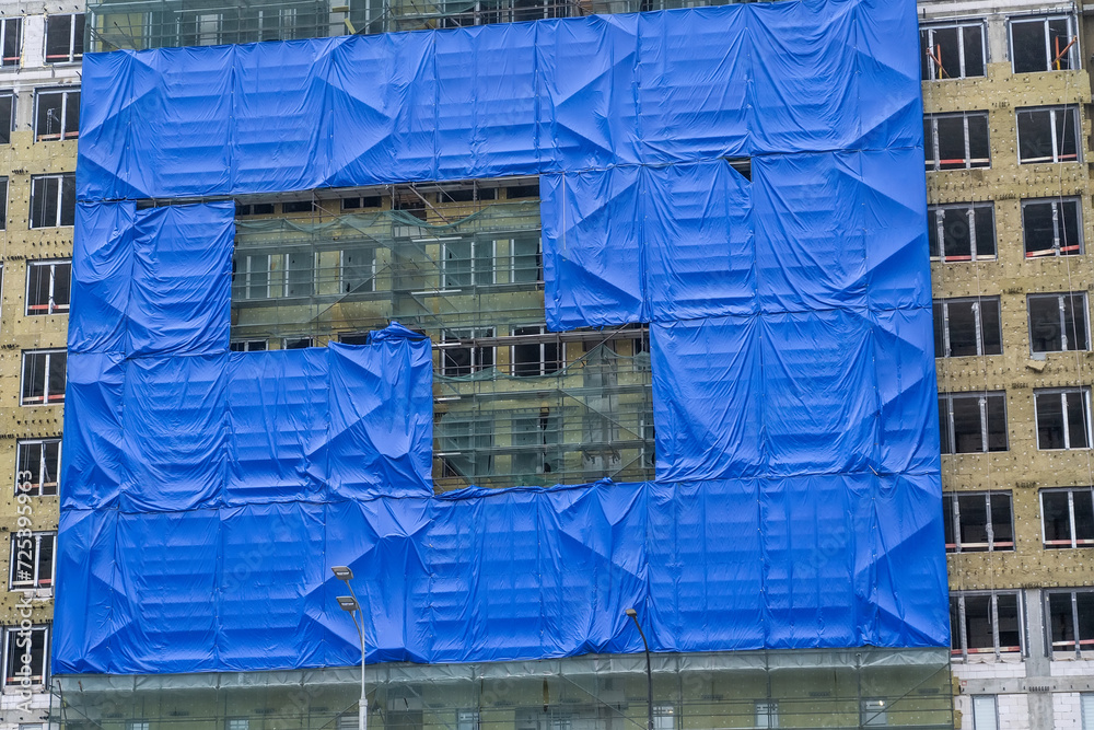 Building is under construction with blue tarps, external thermal ...
