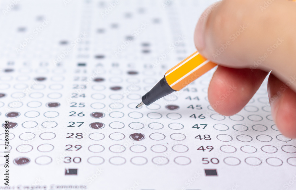 Hand filling out an exam answer sheet with a pen, concept for public ...