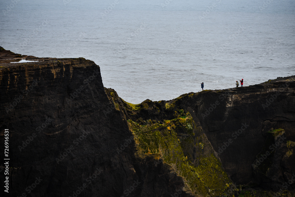 Hikers on the narrow cliffside path to the black volcanic Dyrholaey ...
