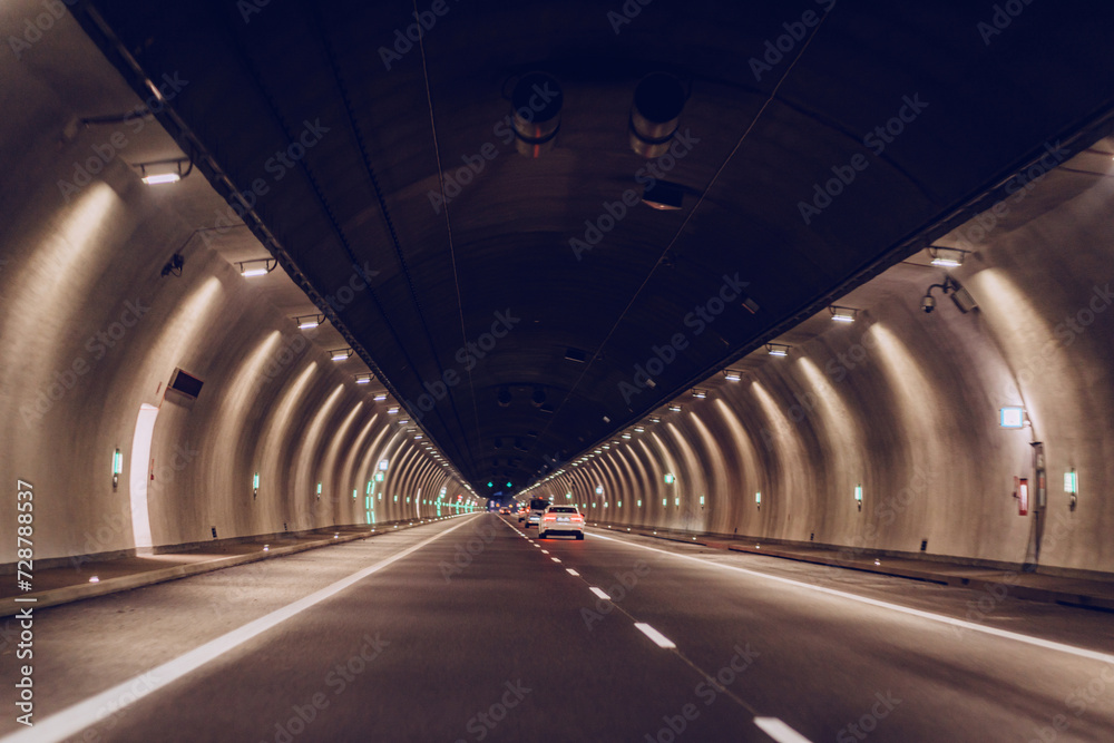 Underground asphalt road tunnel illuminated with yellow lights at night ...