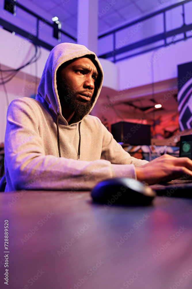 Confused african american criminal using computer for coding illegal ransomware. Concerned young ...