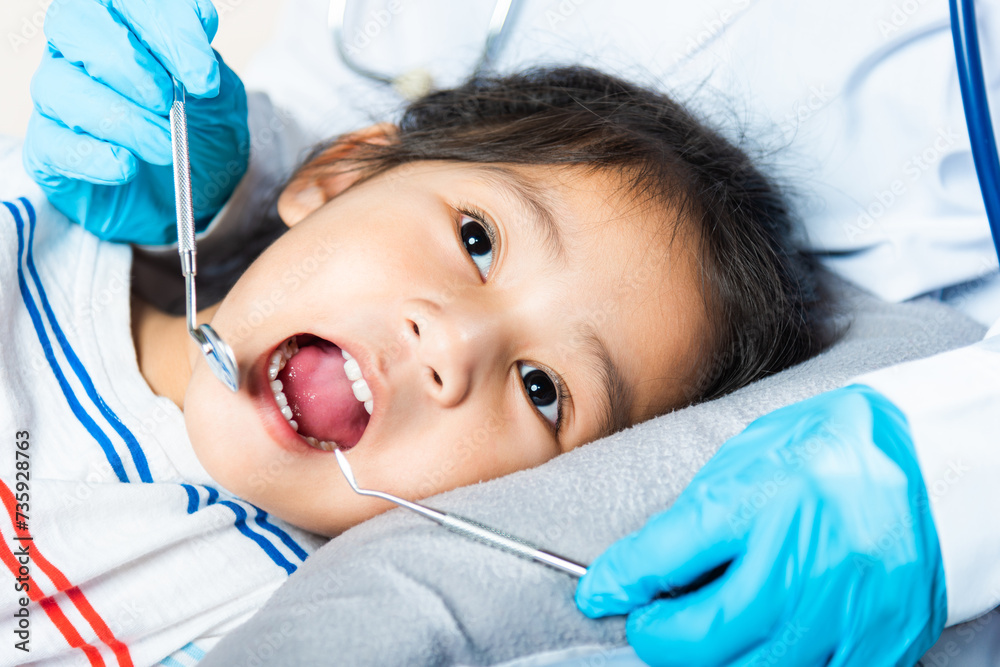 Dental kid health examination. Doctor examines oral cavity of little child uses mouth mirror to ...