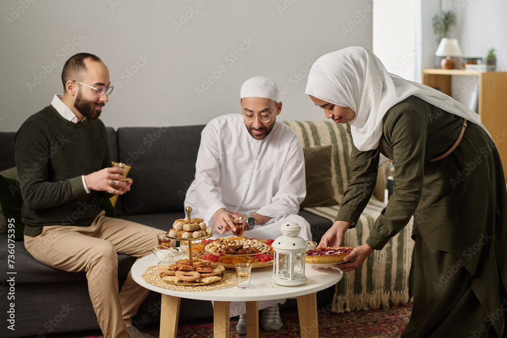 Young Muslim woman in hijab bending over table with appetizing homemade ...