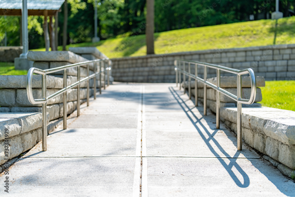 Outdoor, exterior gray concrete ramped sidewalk with stainless steel ...