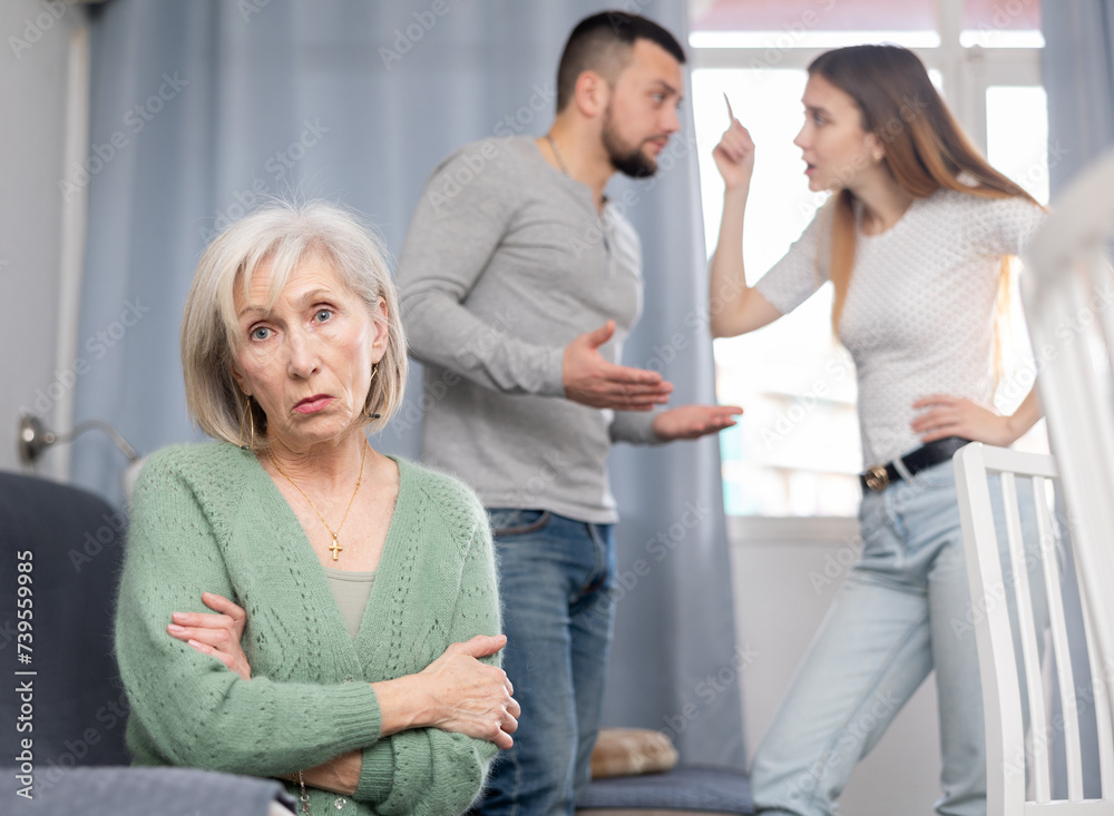Old woman ignoring her daughter and son-in-law standing behind and arguing with each other at ...