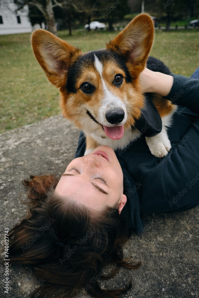 Young woman lies on a concrete slab in the park and hugs her dog. Welsh ...