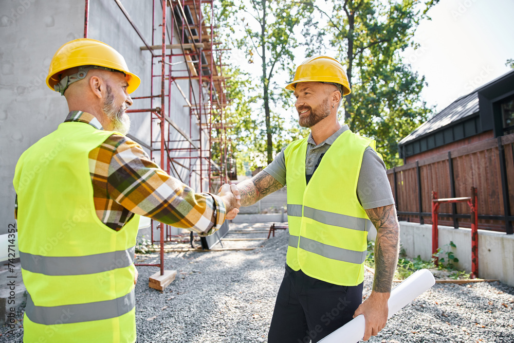 cheerful construction workers shaking their hands and smiling at each ...