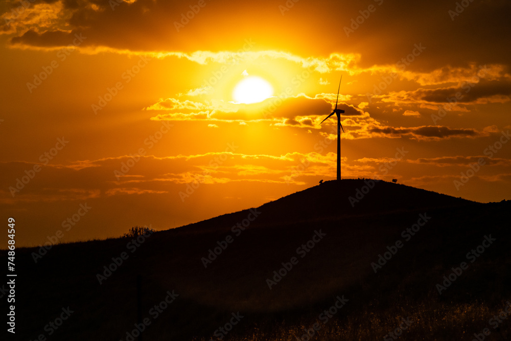 Aerogenerador en el horizonte sobre una colina al atardecer. el sol al ...