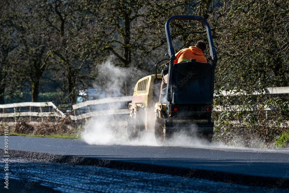 Residential street repaving project, worker on a steamroller compacting ...