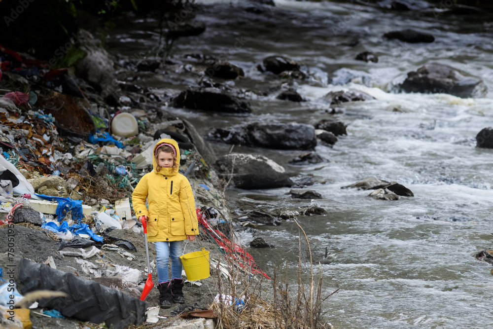 Little girl picking up litter, debris along riverbank in nature. Water ...