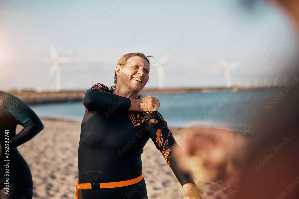 Smiling woman taking off a wetsuit with her open water swimming group ...