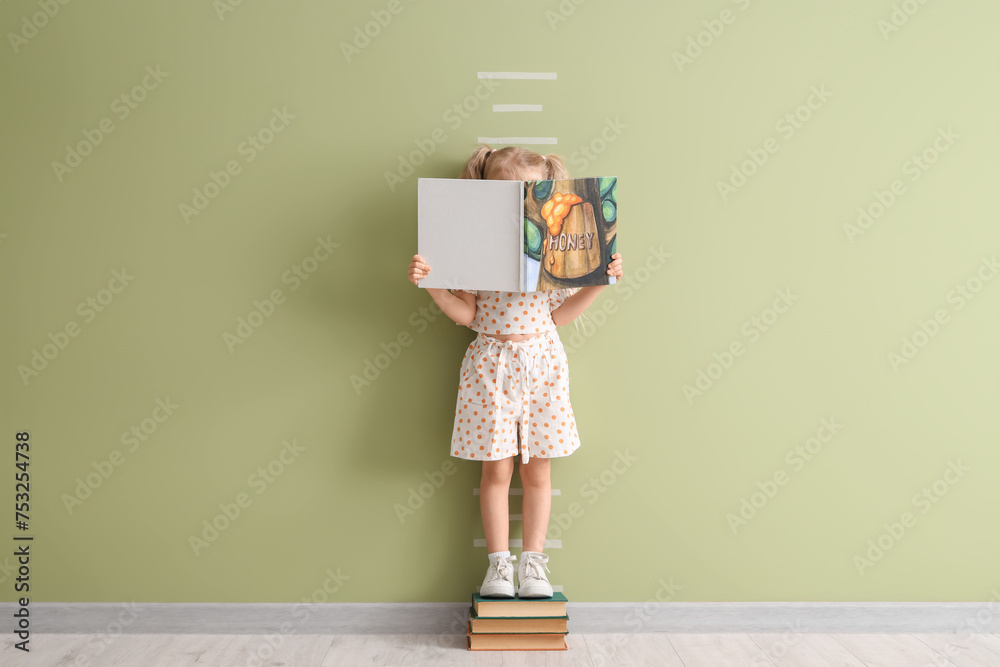 Cute little girl with fairy tale book measuring height near green wall ...
