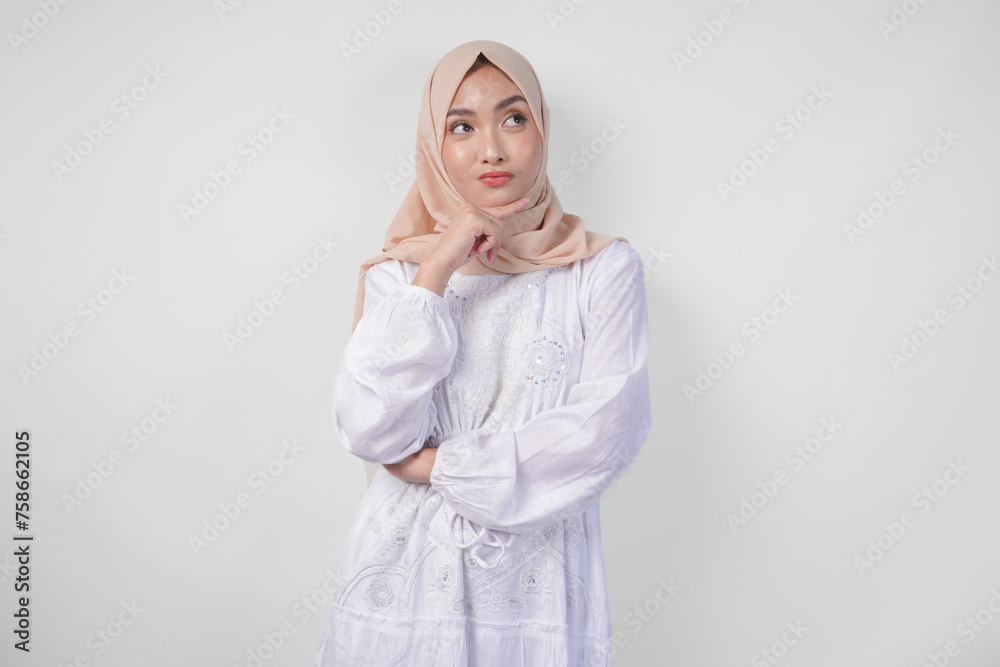 Thoughtful young Asian Muslim woman wearing white dress and hijab ...
