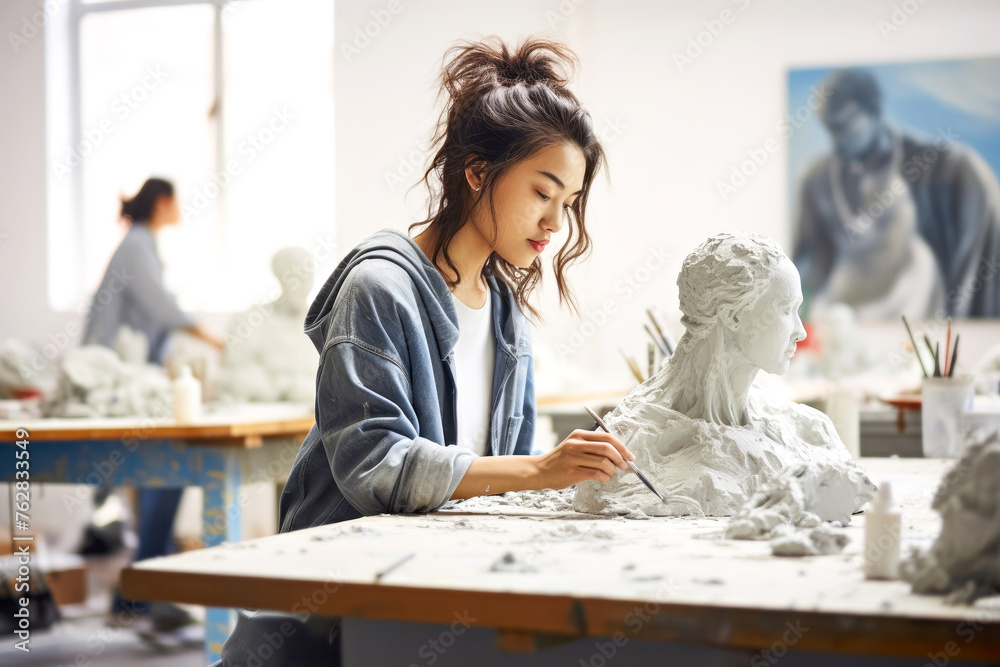 Young Asian female artist concentrates on sculpting, molding a ...