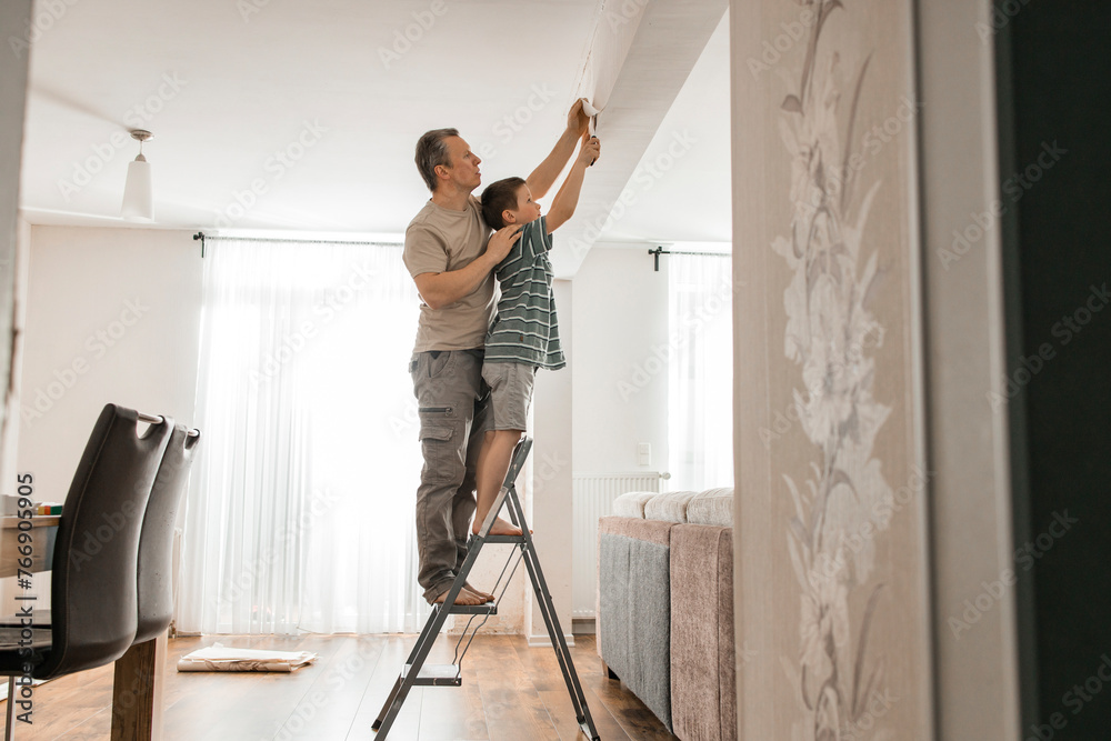 Son and father peeling old wallpaper standing on step ladder at home 素材 ...