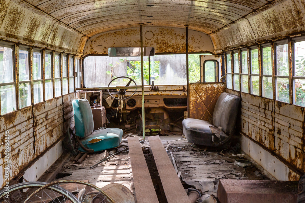 the empty inside of a rusty old yellow school bus overgrown with weeds ...