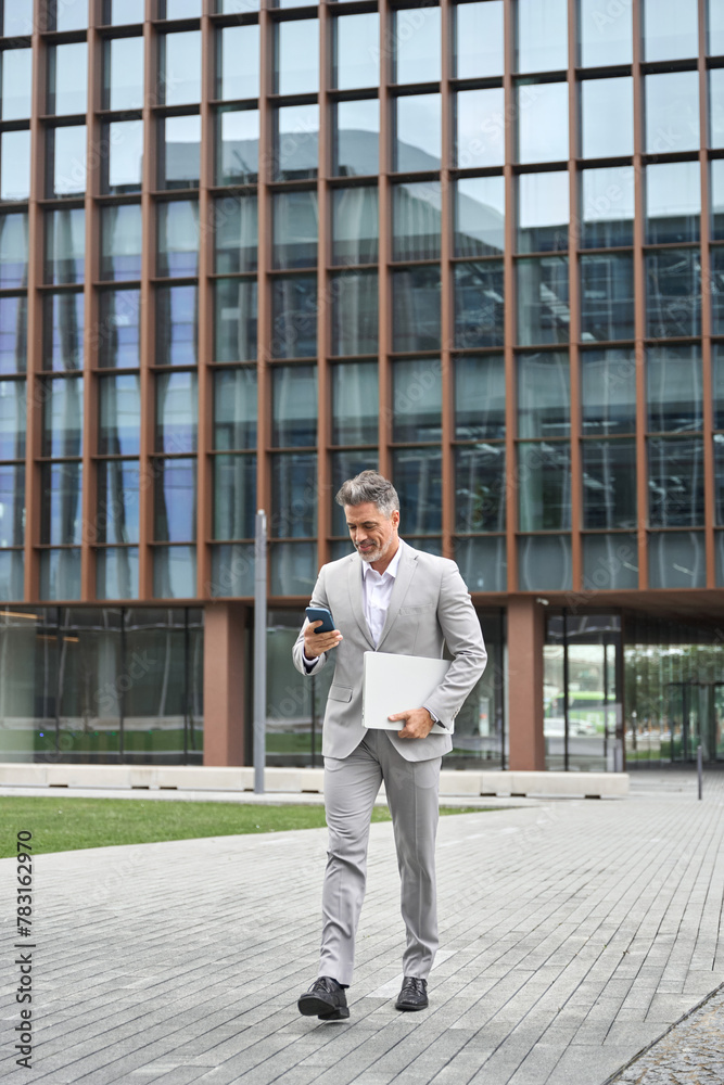 Middle aged businessman using phone walking on city street, busy older business man leader ...