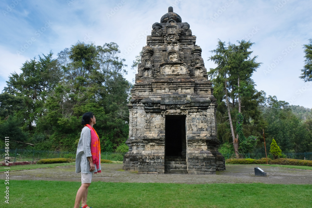 Side view: A female tourist is looking at Bima temple in Dieng Plateau ...
