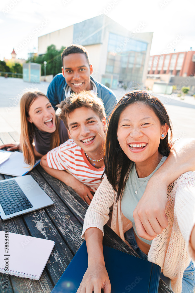 Vertical group of happy teenagers smiling, taking a selfie portrait together during a student ...