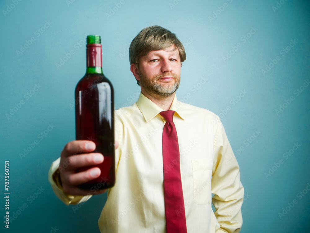 Office worker on blue wall background holding open bottle of red wine ...