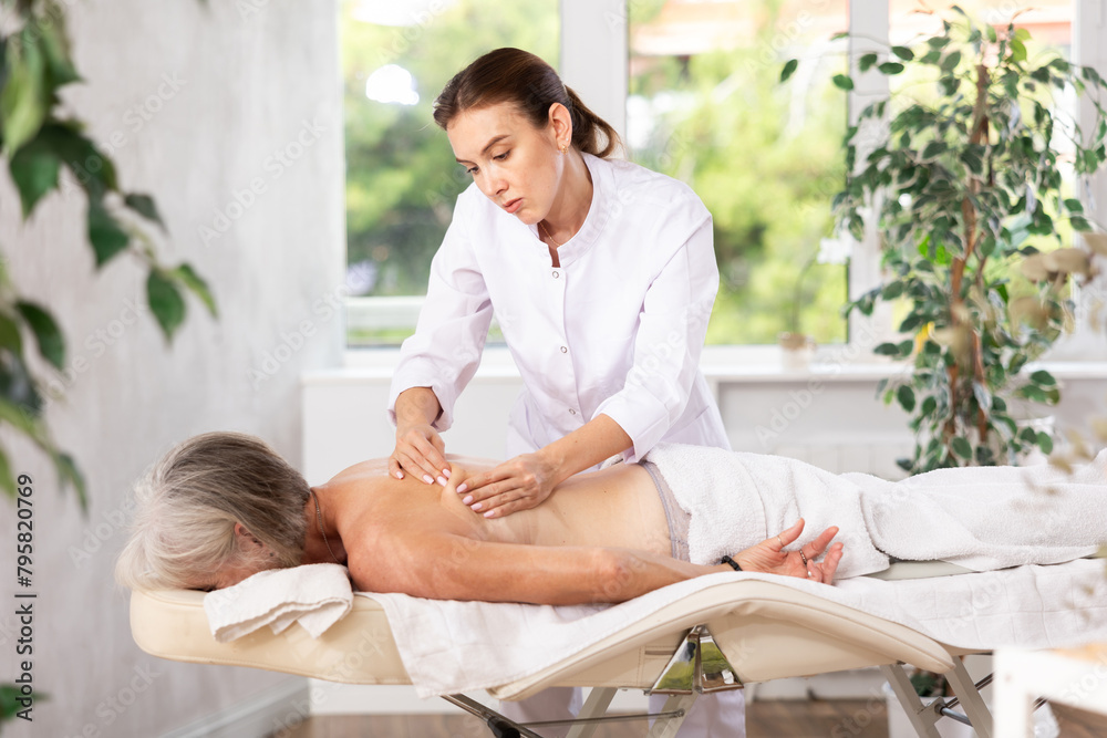 Middle-aged woman actively rubs shoulders and back of elderly female ...