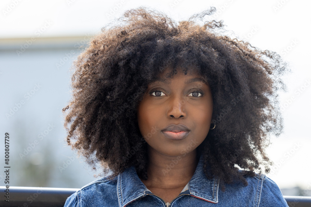 The photograph captures a headshot of a young African woman in a denim ...