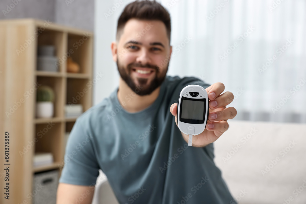 Diabetes test. Smiling man showing glucometer at home, selective focus ...