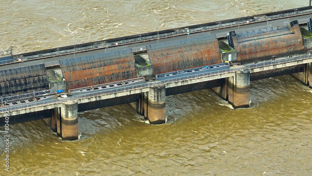 A vast dam extends over the murky waters, cradling a steadfast railway ...
