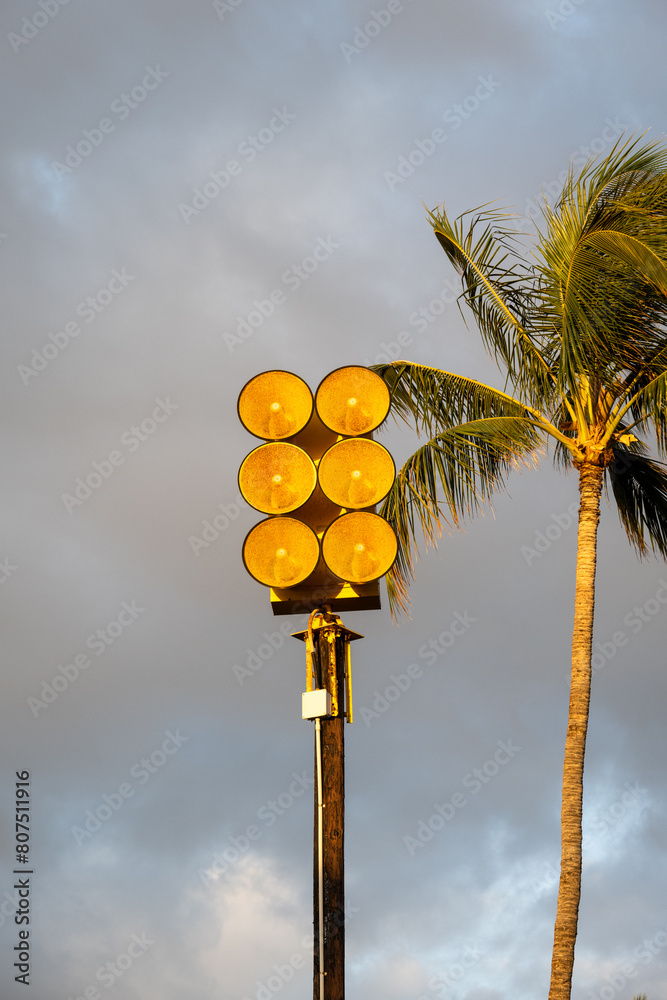 Bright yellow tsunami sirens and palm trees against a cloudy sky at ...
