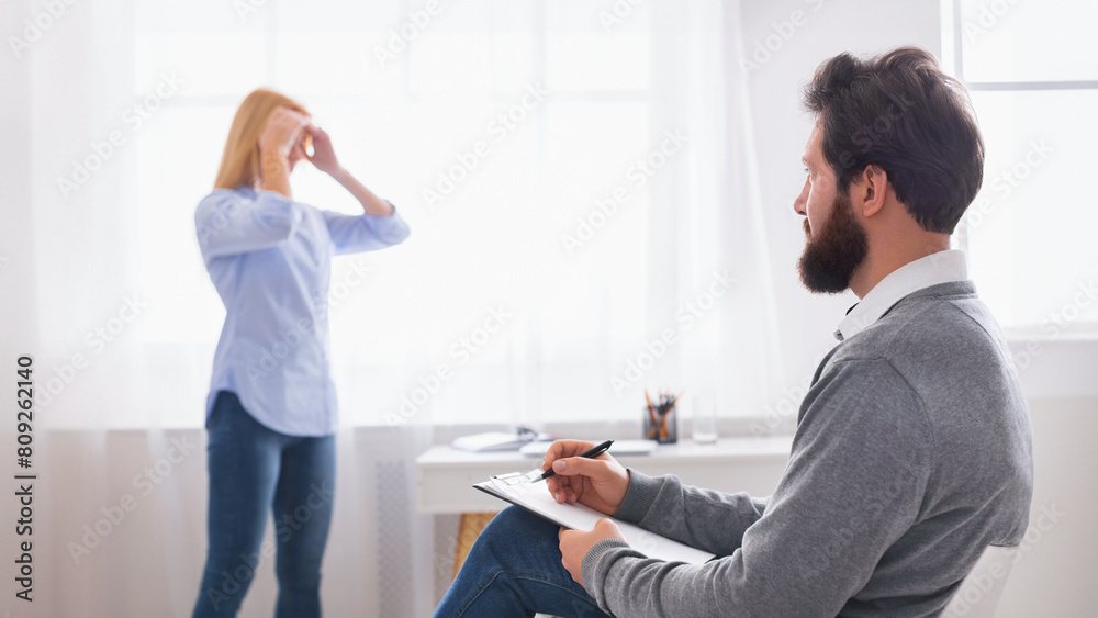 Man therapist is seated, holding a notepad and pen, facing woman client ...