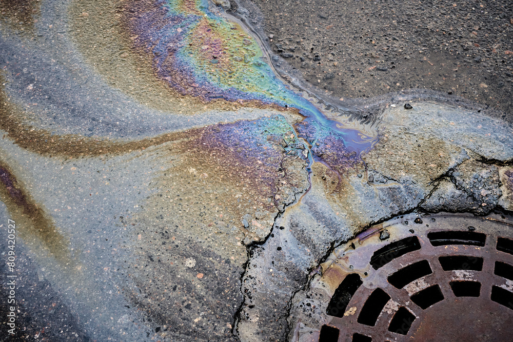 Oil slick on the asphalt road background drains into the storm drain ...